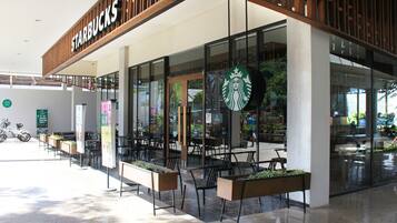 Uma loja Starbucks com área externa, uma bicicleta estacionada e uma placa indicando um restaurante próximo.