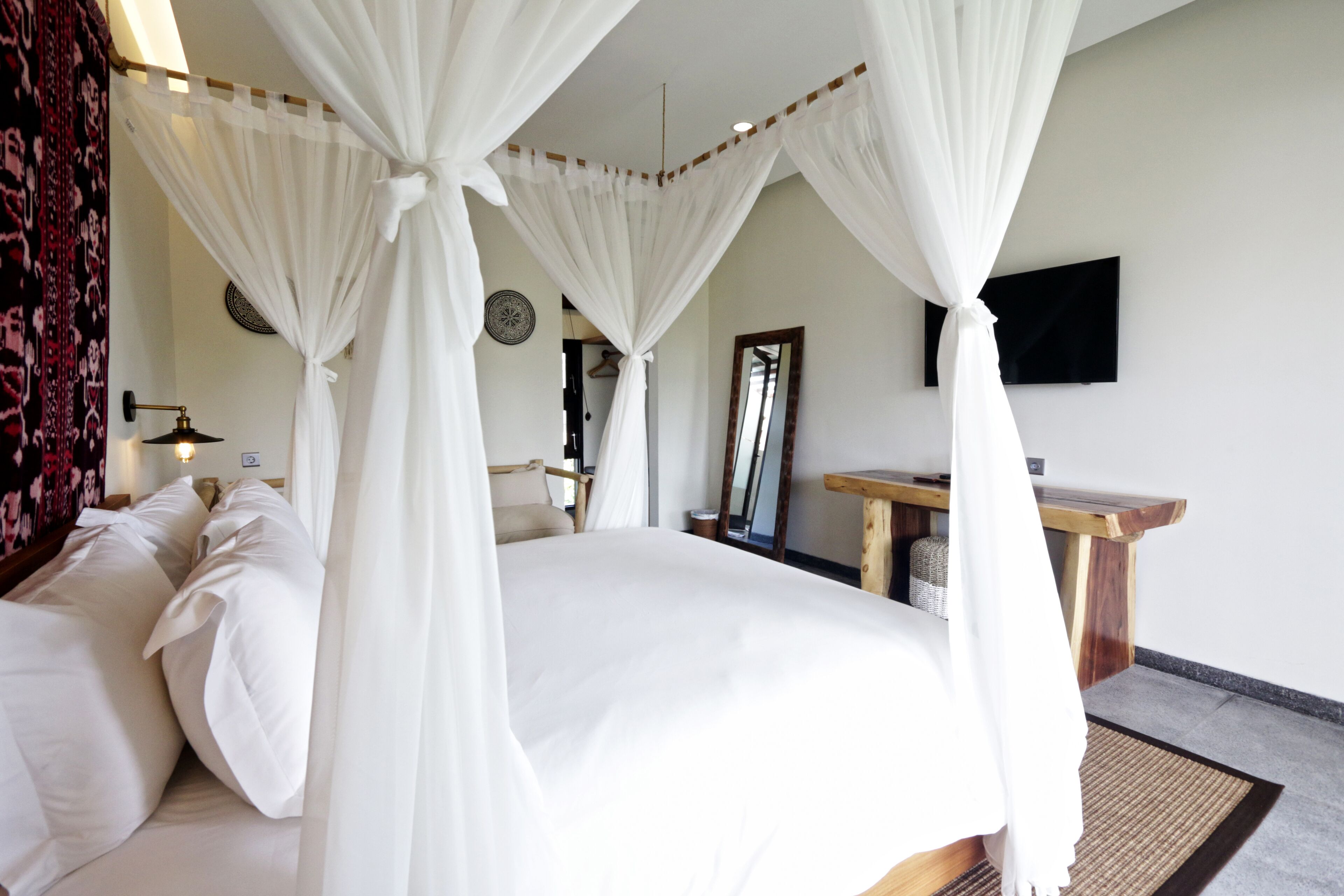 Quarto com cama de dossel, mesa de cabeceira, espelho e televisão na parede.