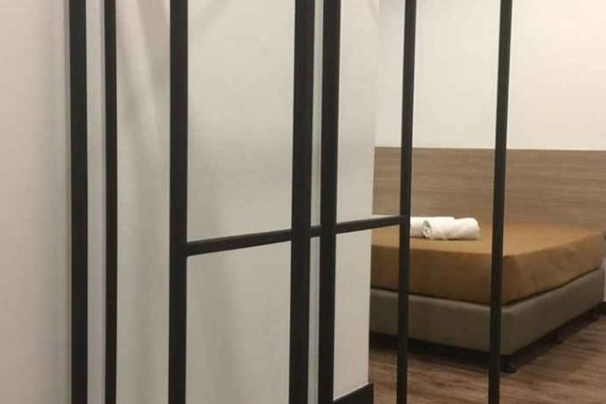Quarto com cama, cabeceira de madeira e divisória de metal preta.