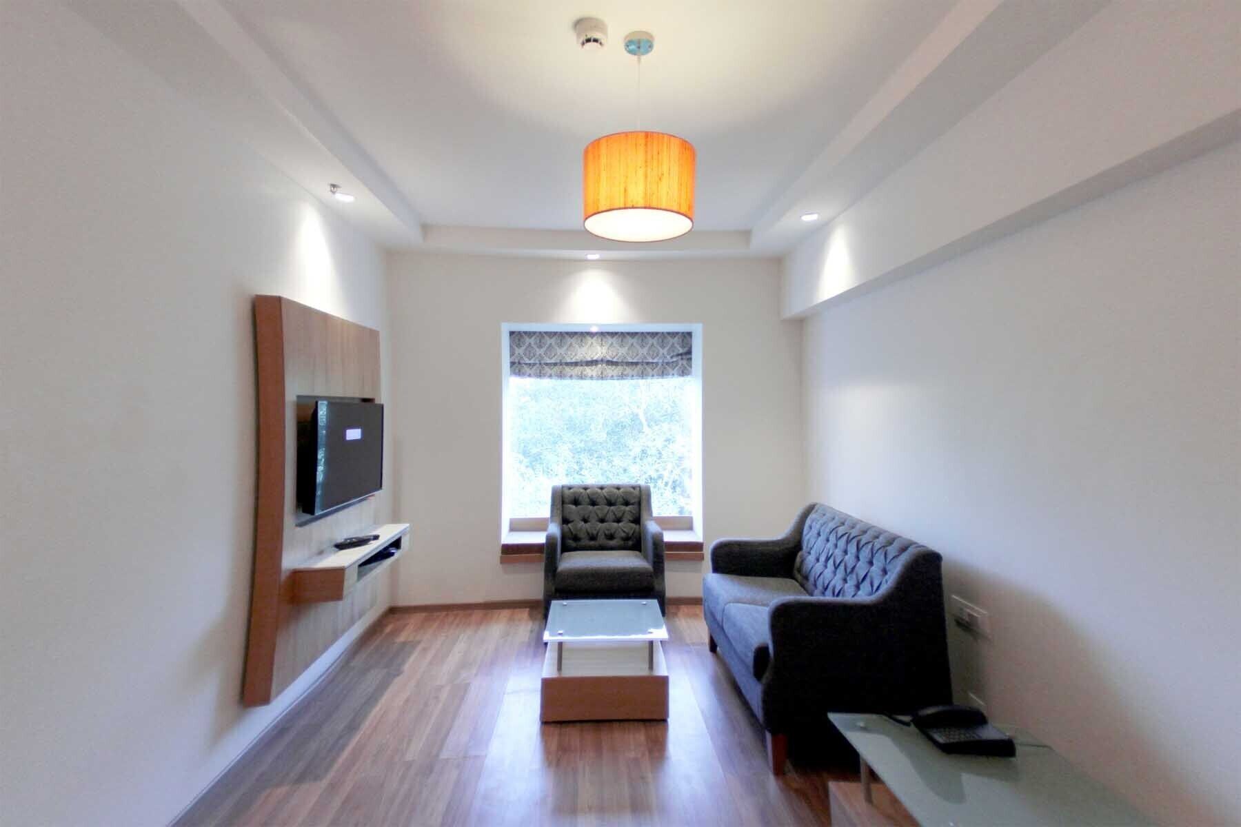 Uma sala de estar moderna com uma televisão de tela plana, um sofá cinza, uma mesinha de centro e piso de madeira.