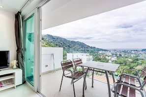 Uma varanda com mesa, cadeiras, uma televisão e porta de vidro que dá para a vista da cidade.