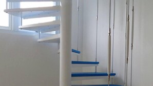 Uma escadaria em espiral com degraus azuis e paredes brancas, que leva a um andar superior.