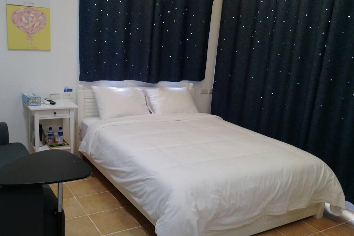 Quarto com cama, mesa de cabeceira com abajur, cadeira e uma pequena mesa.