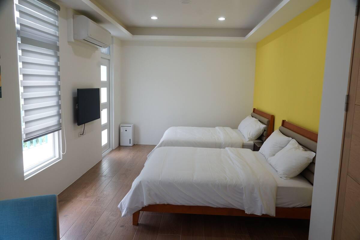 Quarto com duas camas, televisão de tela plana na parede e aparelho de ar condicionado.