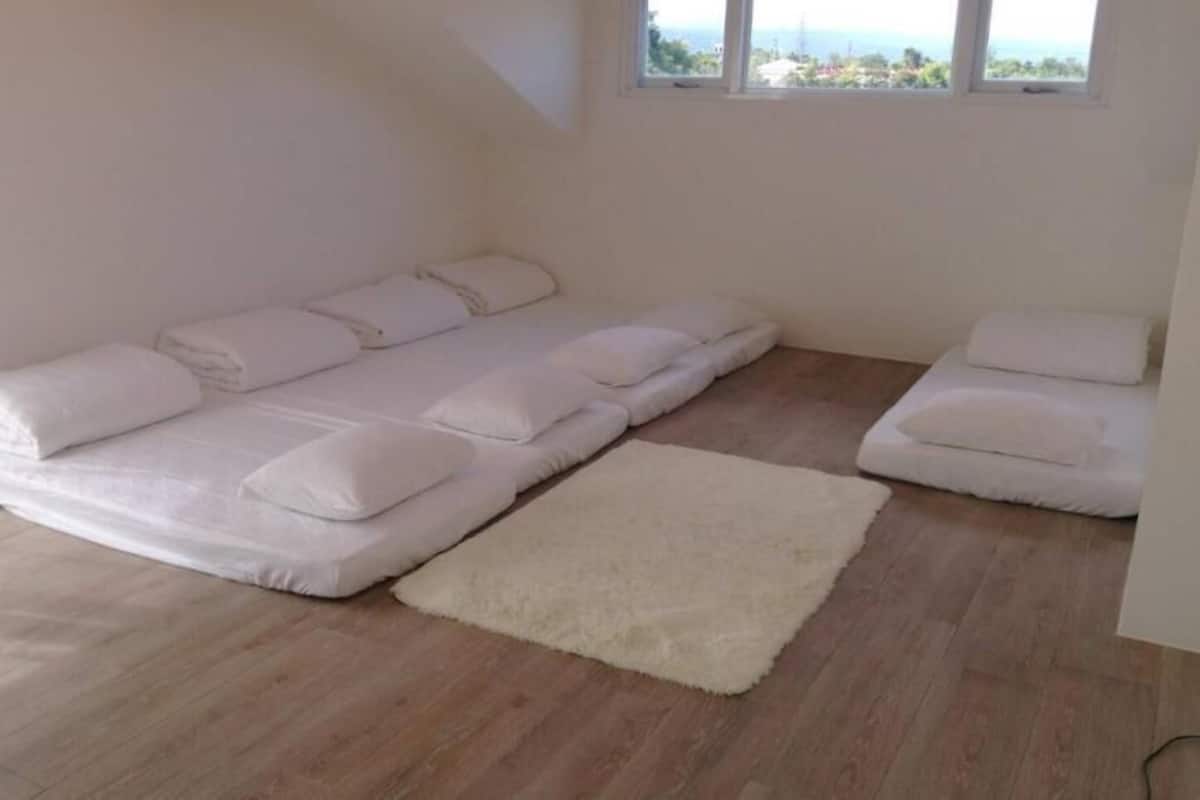 Quarto com um amplo sofá branco, um tapete branco e vista para o exterior através de uma janela.