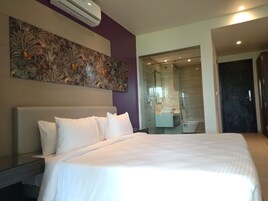 Quarto de hotel moderno com uma cama grande, banheiro com box de vidro e ar-condicionado fixado na parede.