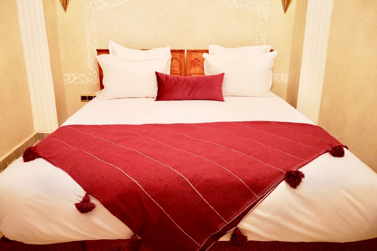 Uma cama bem arrumada com roupa de cama branca e vermelha, um cobertor vermelho e uma cabeceira de madeira.