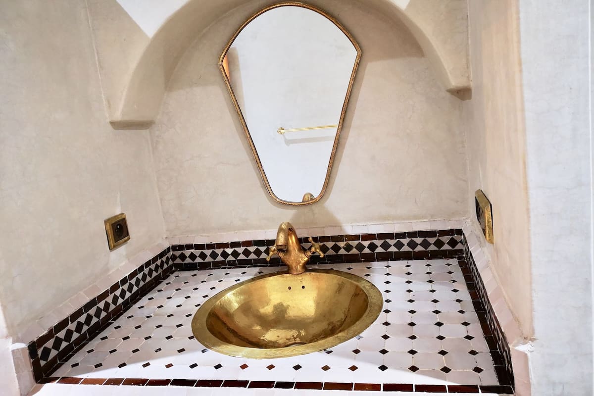 Uma casa de banho com lavatório dourado, espelho com moldura dourada e pavimento em azulejos estampados.