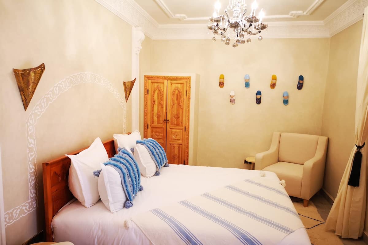 Um quarto com uma cama grande, um guarda-roupa de madeira, um candelabro e uma cadeira.