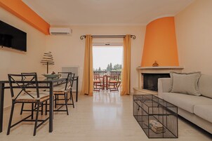 Uma sala de estar com sofá, lareira, área de refeições com cadeiras e mesa, e varanda com vista.