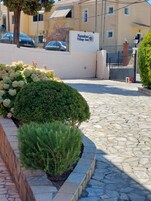 Uma entrada pavimentada com uma placa do Nanakas Village Inn, uma área cercada e sebes bem cuidadas.