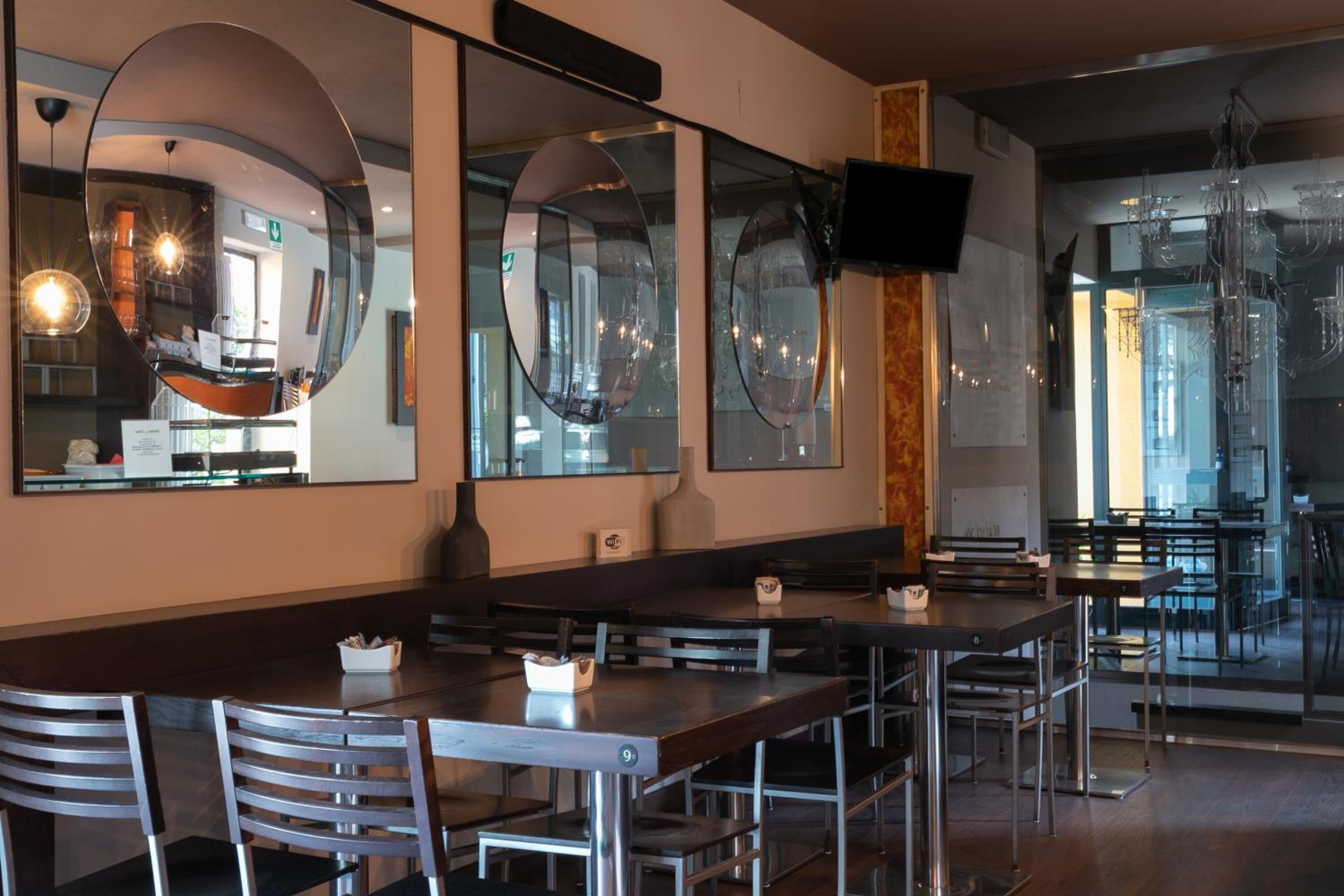 Um restaurante moderno com um balcão extenso, várias áreas de estar e espelhos grandes nas paredes.