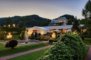 Um hotel moderno com um amplo espaço de refeições ao ar livre, uma fonte e jardins bem cuidados.