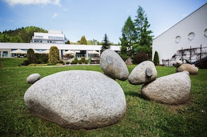 Um edifício moderno com telhado plano e amplas janelas, rodeado por um jardim bem cuidado com várias pedras grandes.