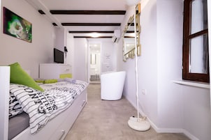 Quarto com cama, televisão, espelho e janela.