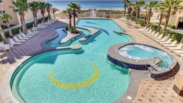 Uma área de piscina com design em formato de crescente lunar, cadeiras de lounge, palmeiras e vista para o oceano.