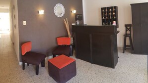 Quarto com parede marrom escura, ar condicionado branco, espelho, mesa pequena com abajur e área de bar com chaveiro.