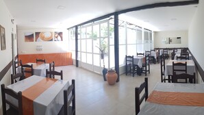 Um restaurante com várias mesas e cadeiras, janelas amplas e um balcão.
