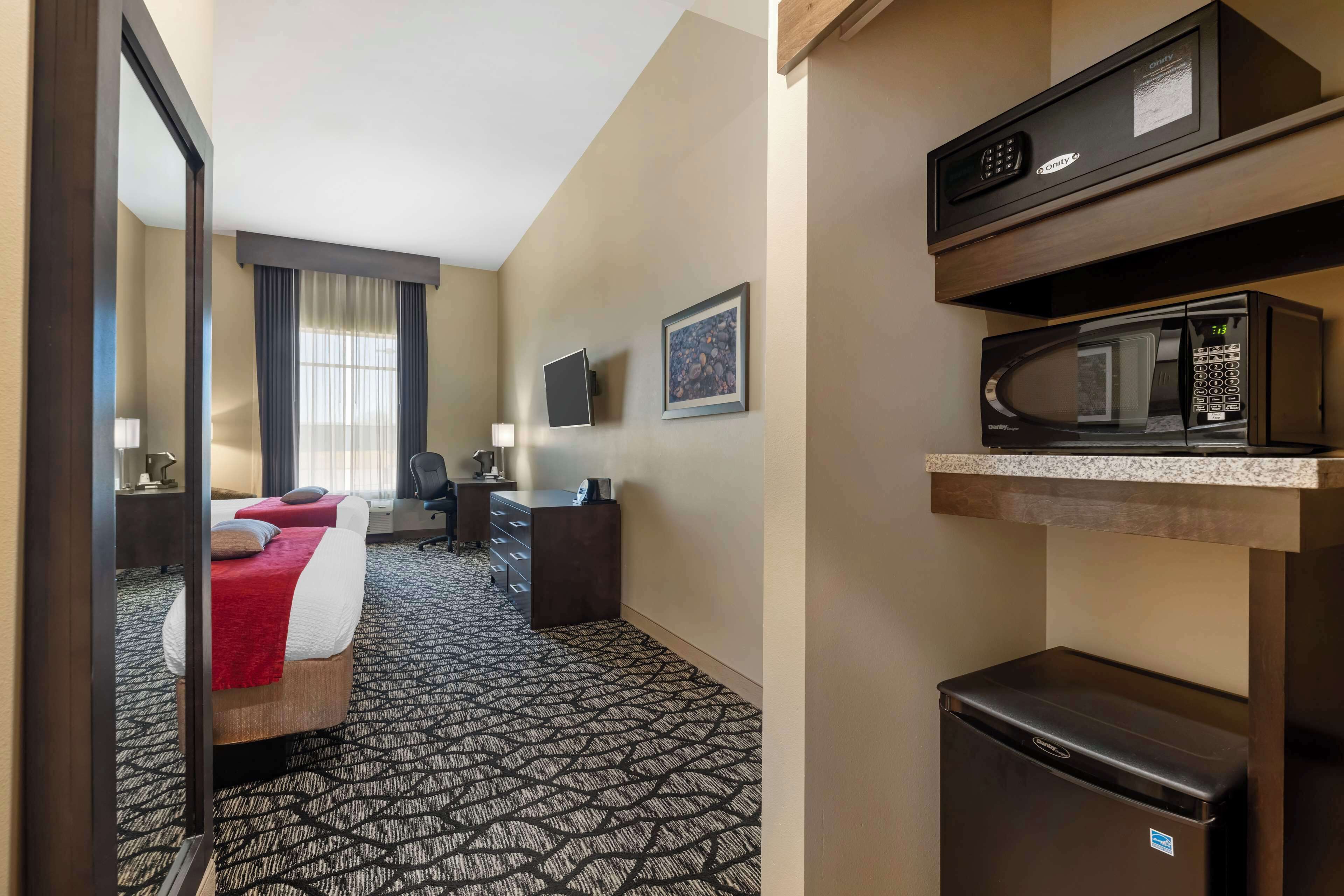 Quarto de hotel com cama, escrivaninha, cadeira, micro-ondas e geladeira.
