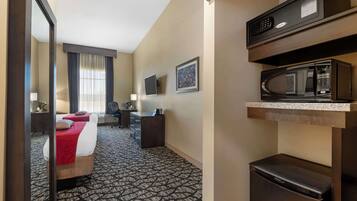 Quarto de hotel com cama, escrivaninha, cadeira, micro-ondas e geladeira.