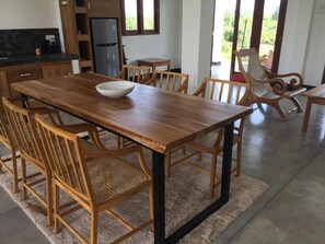 Uma área de refeições com uma mesa e cadeiras de madeira, uma tigela sobre a mesa e uma cozinha ao fundo.