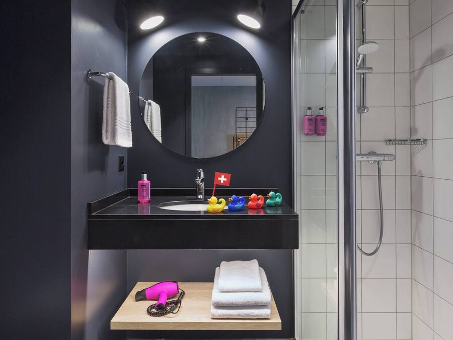 Casa de banho moderna com lavatório preto, espelho redondo, lavatório branco e chuveiro.