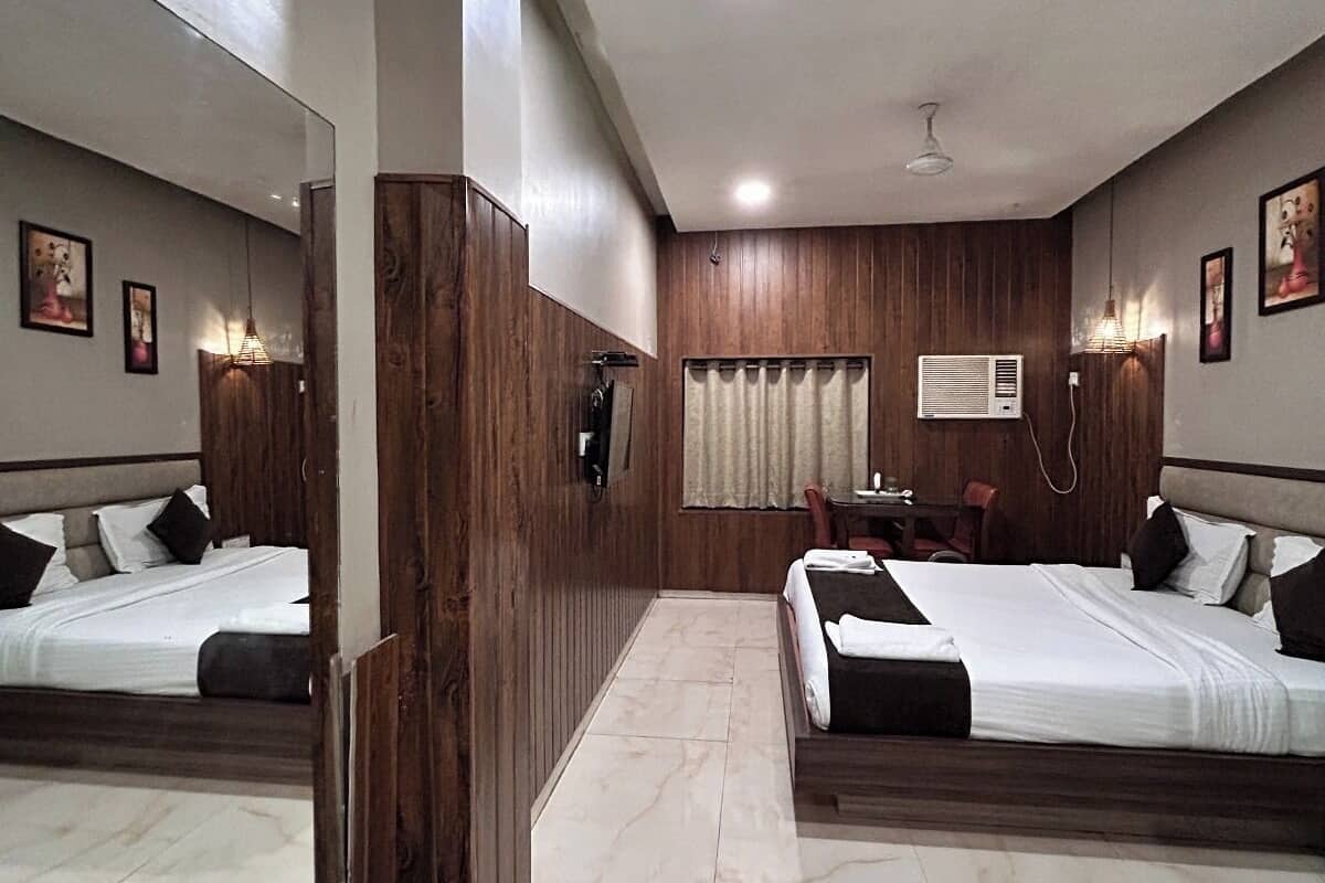 Quarto de hotel com duas camas, parede de destaque em madeira, espelho, ventilador de teto e janela com cortinas.