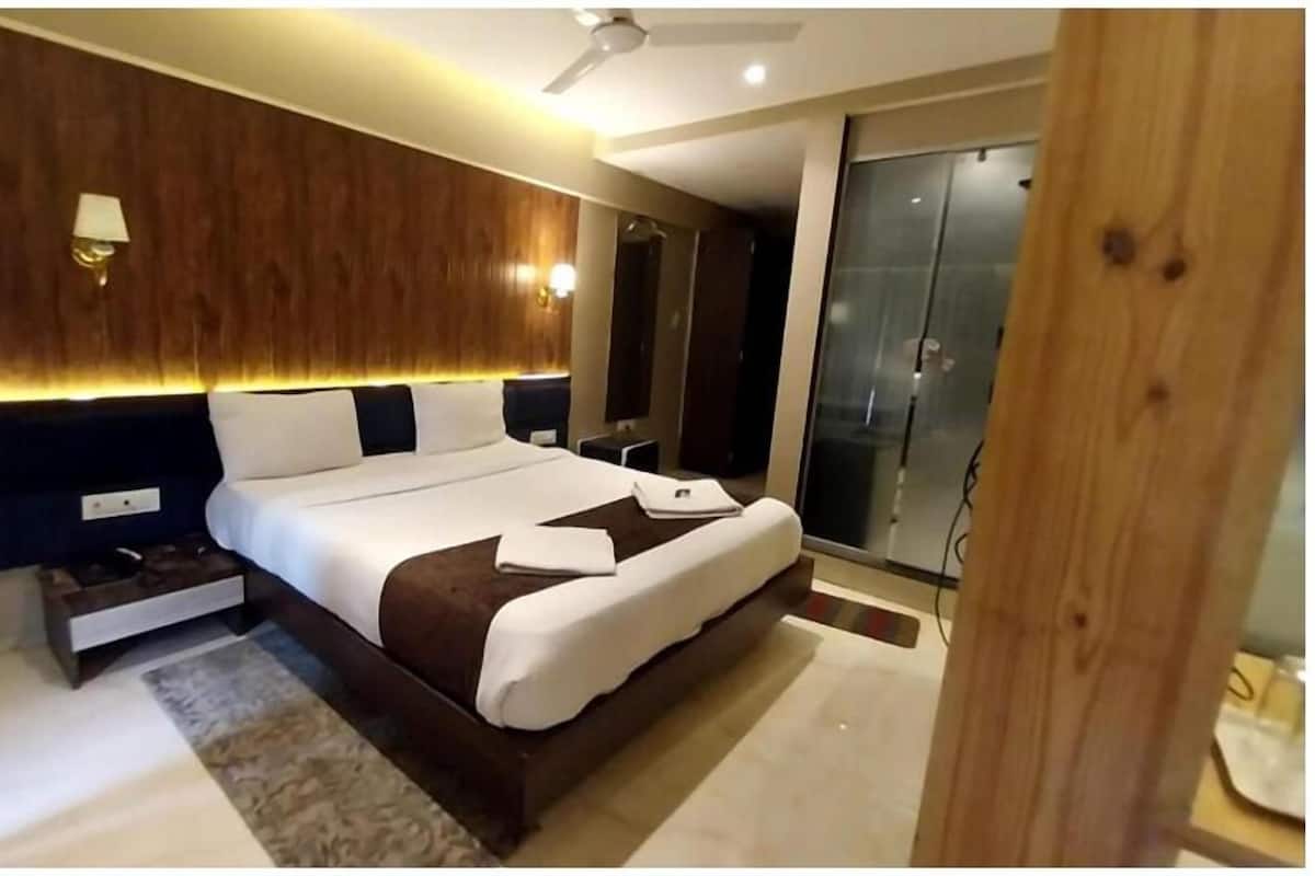 Quarto de hotel moderno com uma cama grande, uma mesinha de cabeceira, um armário com portas deslizantes e uma luminária na parede.