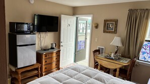 Quarto de hotel com cama, escrivaninha com luminária, geladeira, micro-ondas, televisão e porta que dá para uma varanda.