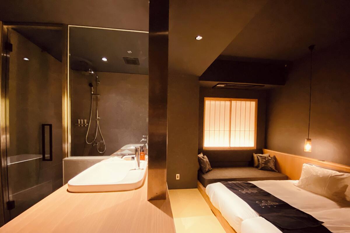 Quarto de hotel moderno com chuveiro, cama, janela e mesa de cabeceira.