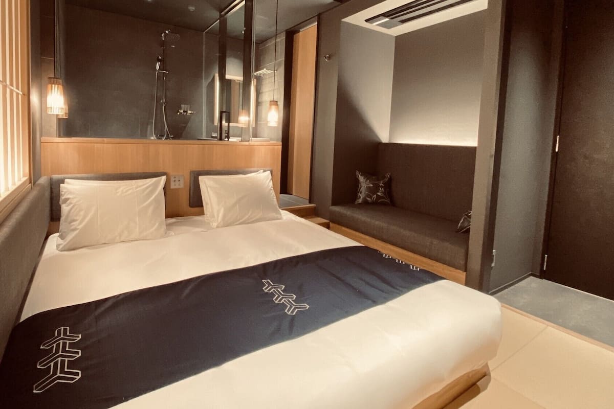 Quarto de hotel moderno com uma cama grande, área de estar e chuveiro.