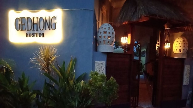 Um edifício com um letreiro que diz "GEDHONG HOSTEL" e uma entrada com telhado de palha.