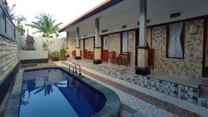 Uma área de piscina com um deck ladrilhado, uma piscina pequena e mobiliário de exterior.