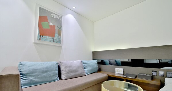 Quarto de hotel moderno com sofá, mesa de cabeceira com abajur e um quadro na parede.