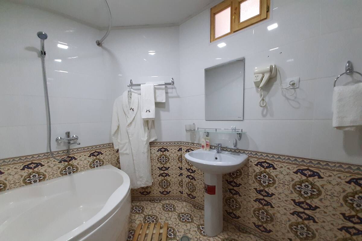 Casa de banho com banheira, lavatório, espelho e azulejos estampados.