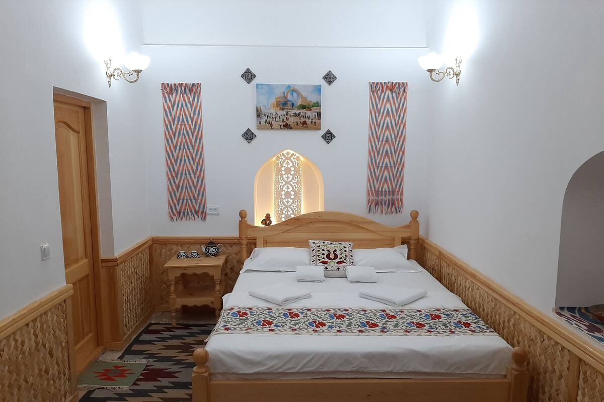 Quarto bem arrumado com uma cama de madeira, mesa de cabeceira, um painel decorativo na parede e tapete estampado.