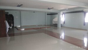 Um quarto amplo e vazio com piso lustroso, ventiladores no teto e uma grande janela com cortinas.