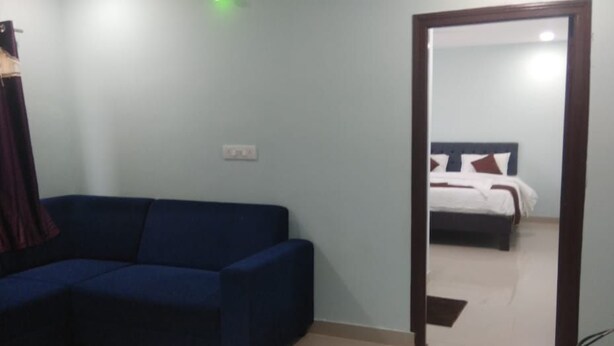 Quarto com um sofá azul, cama com roupa de cama branca e um espelho refletindo o ambiente.