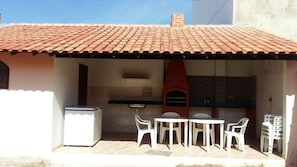 Um pátio com telhado de azulejos, churrasqueira e cadeiras de plástico branco.