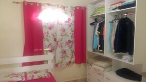 Quarto com cama, guarda-roupa e armário com roupas dobradas.