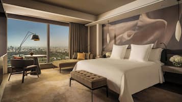 Quarto de hotel moderno com cama grande, área de estar e vista para o horizonte urbano visível pela janela.