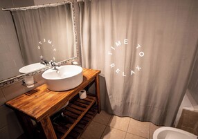 Casa de banho com toucador de madeira, duas pias, um espelho e cortina de chuveiro com texto.