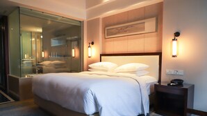 Quarto de hotel moderno com uma cama grande, chuveiro em gabinete de vidro e mesa de cabeceira com abajur.