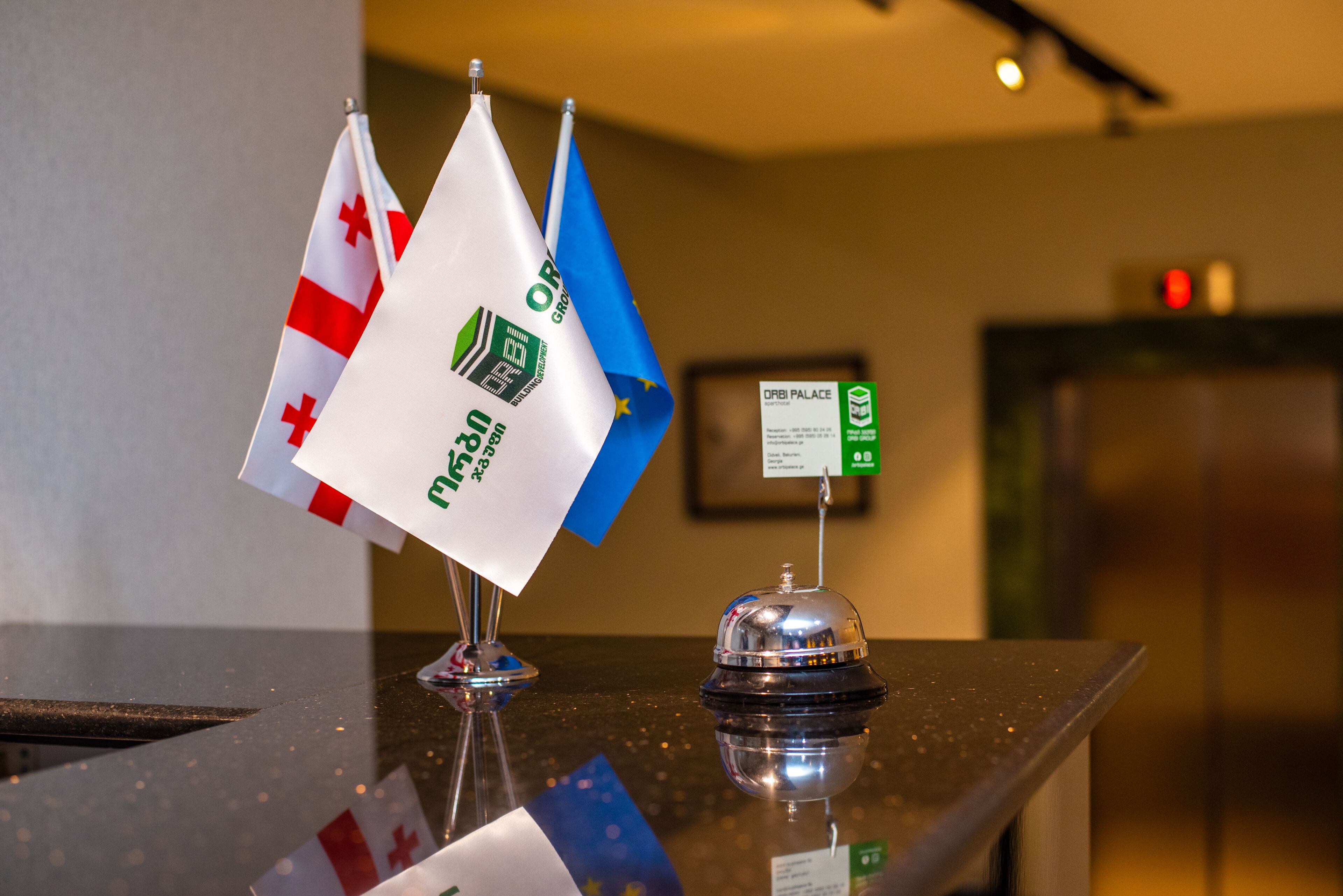 Bancada de recepção com bandeiras, uma placa indicando ORBI PALACE e um sino.