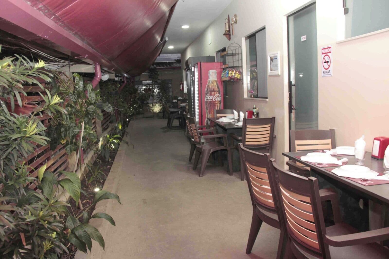 Restaurante com plantas, mesas, cadeiras e refrigerador de Coca-Cola.