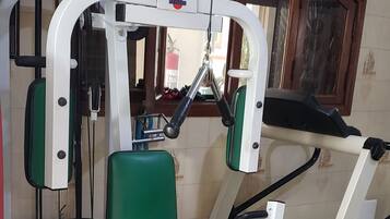Uma academia com esteira, aparelhos de musculação e uma cadeira verde.