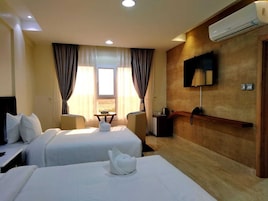 Quarto de hotel com duas camas, televisão fixada na parede e uma pequena mesa com uma cadeira.