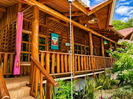 Uma cabana de madeira com varanda, escadas que levam à entrada e um candeeiro suspenso.