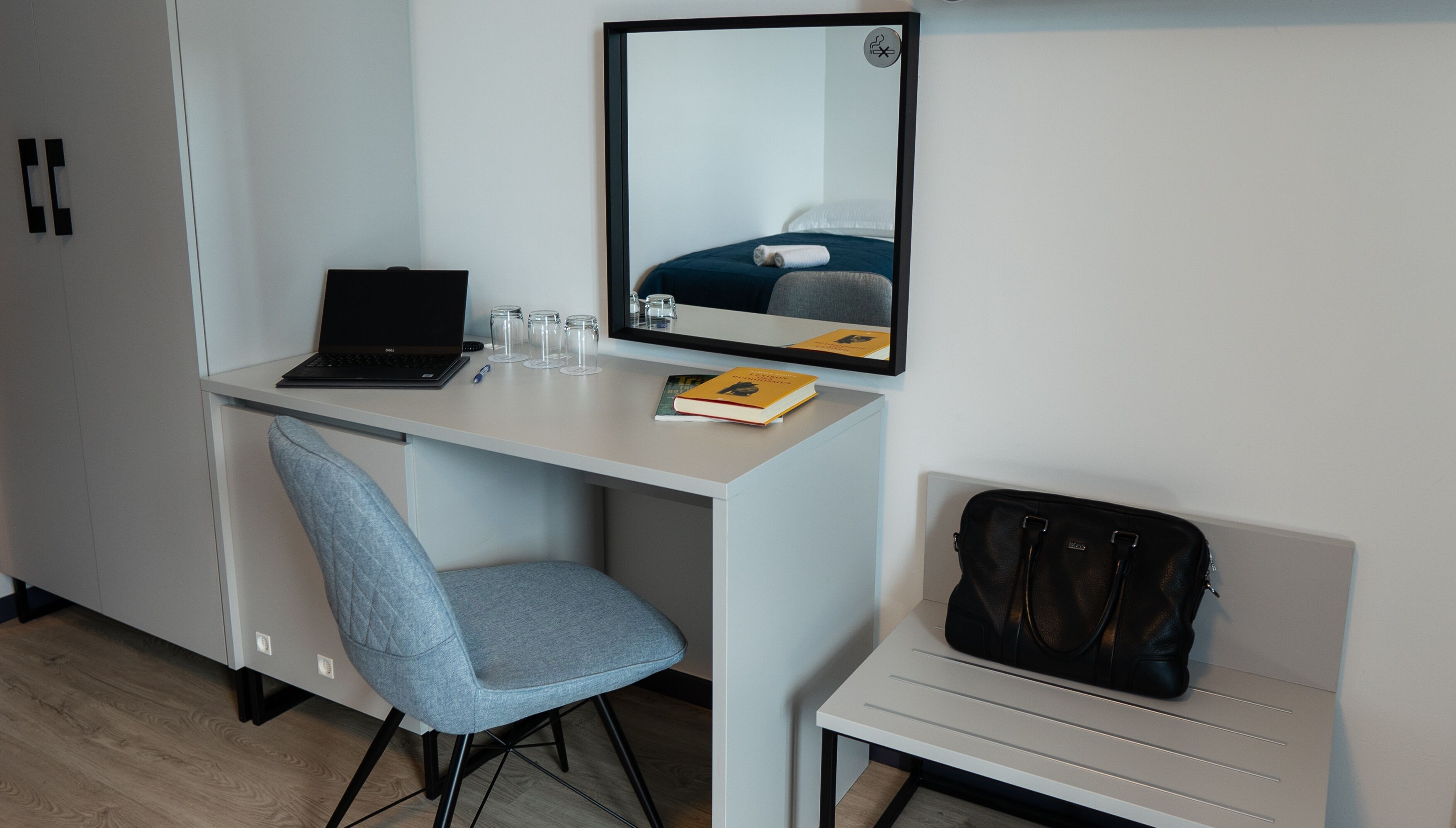 Quarto de hotel pequeno com uma escrivaninha, um laptop, uma cadeira, uma mesa, um espelho e uma bolsa preta.