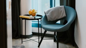 Quarto de canto com uma cadeira azul-turquesa, uma mesa pequena com uma tigela de frutas e vista através de uma janela grande com moldura azul.